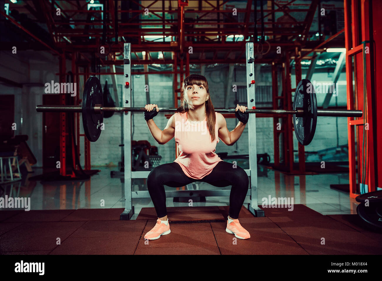 Gorgeous young fitness woman crouch and doing squad exercise with a bar ...