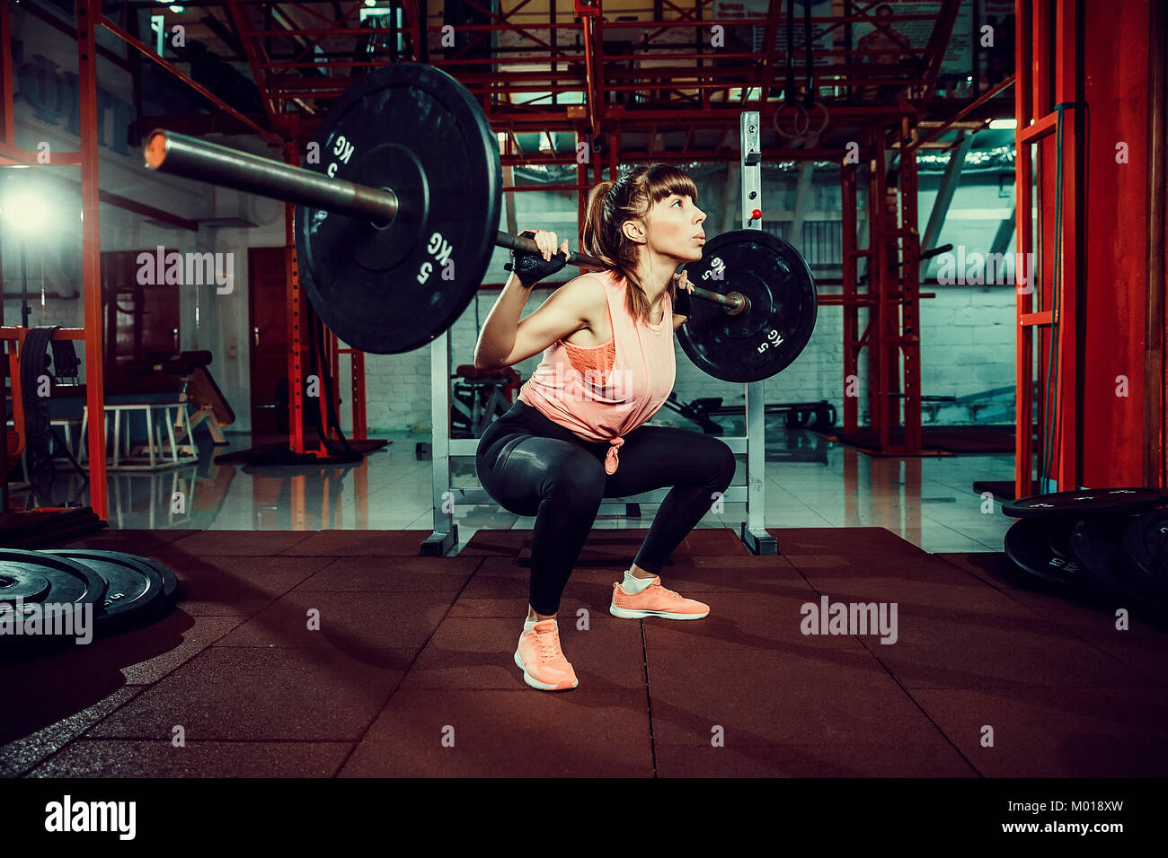 Gorgeous young fitness woman crouch and doing squad exercise with a bar ...