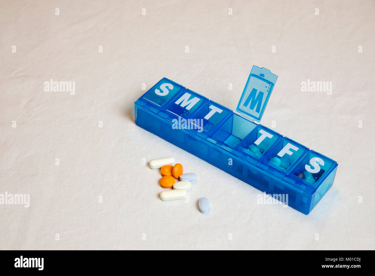 Assorted pills next to blue plastic pill weekly organizer on white ...