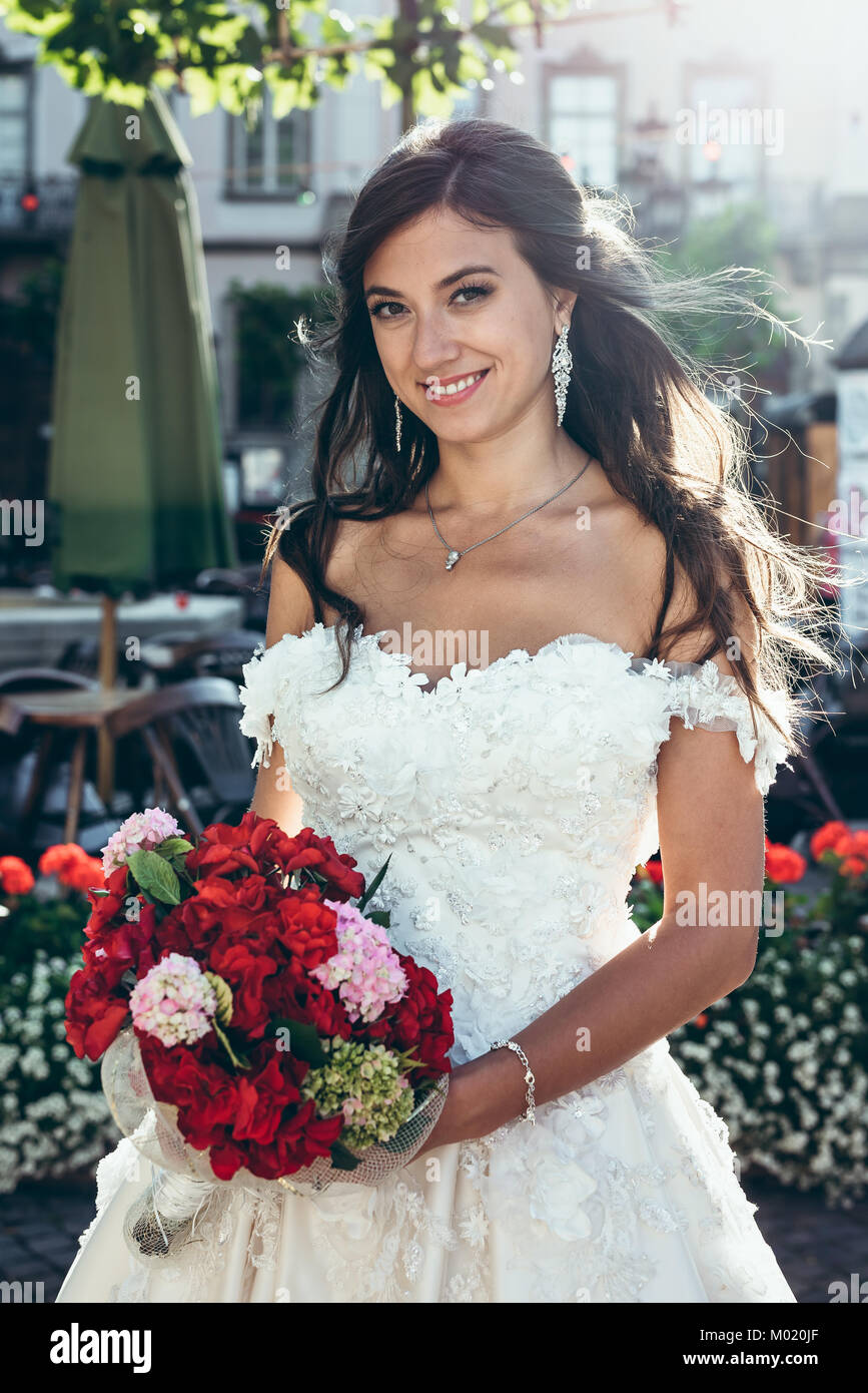 Pretty bride with charming smile hold the wedding bouquet of red and ...