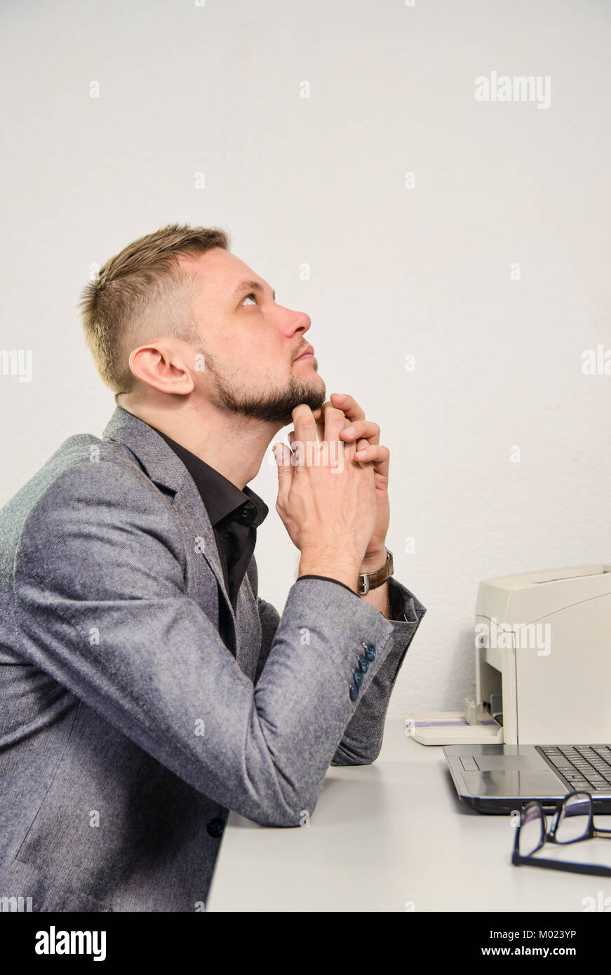 man with chin on hands thoughtfully looking upwards sitting at table ...