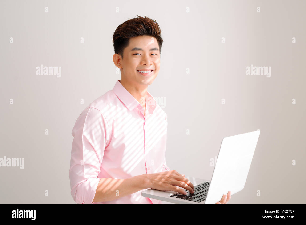 Handsome asian man standing with laptop on gray background Stock Photo ...