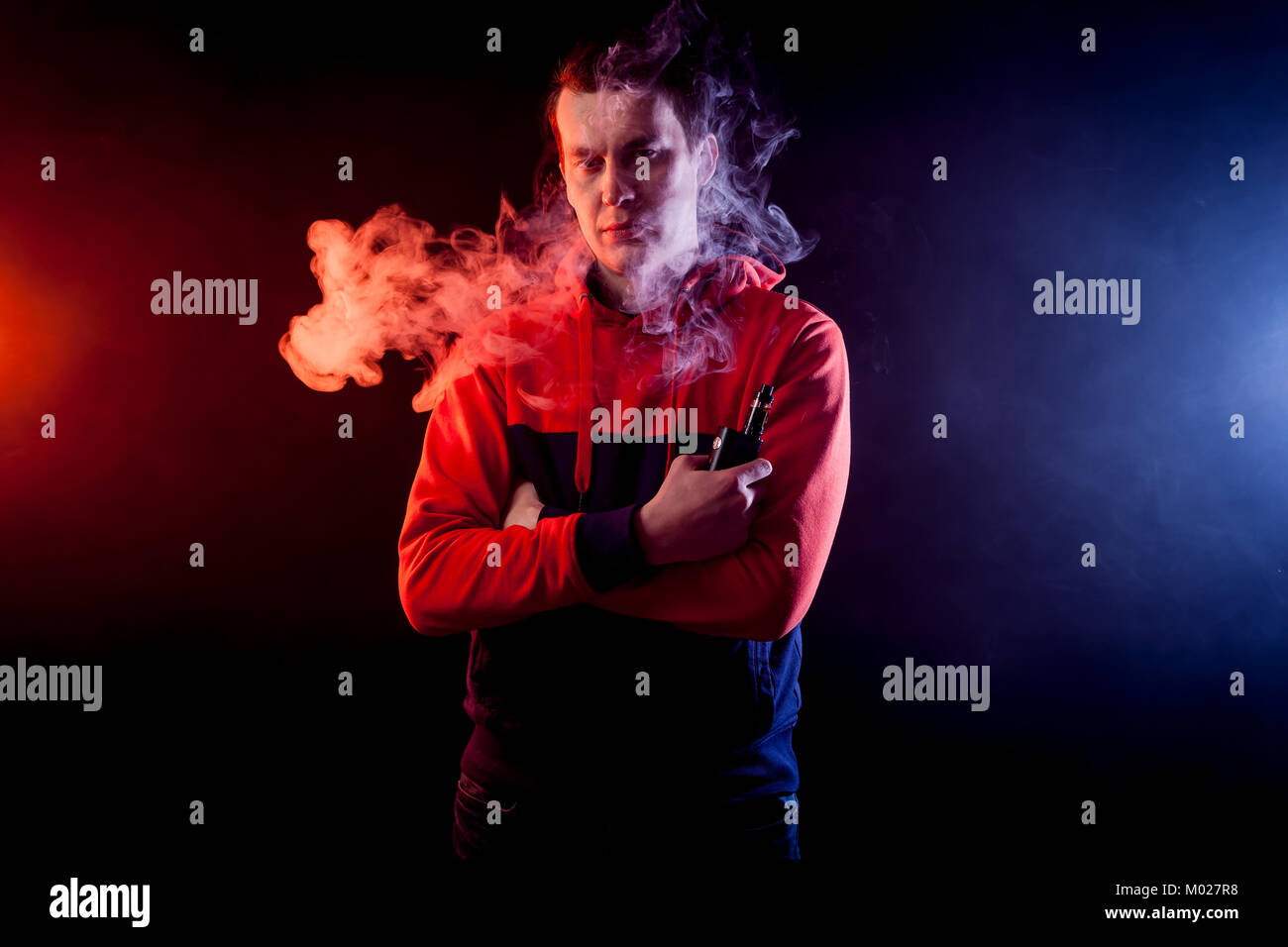 Portrait of a young handsome man holding a vape and exhaling a large ...