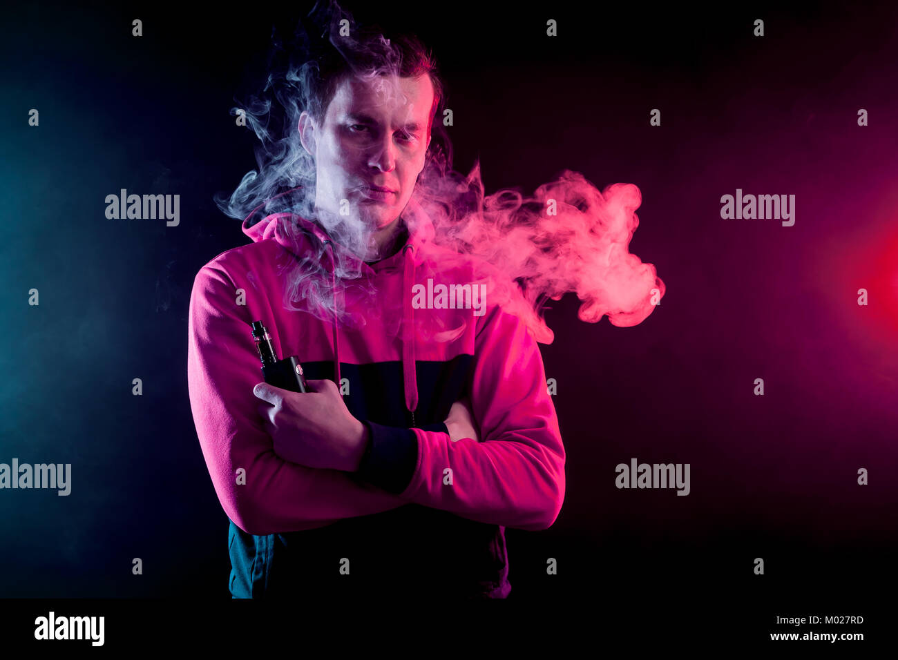 Portrait of a young handsome man holding a vape and exhaling a large ...