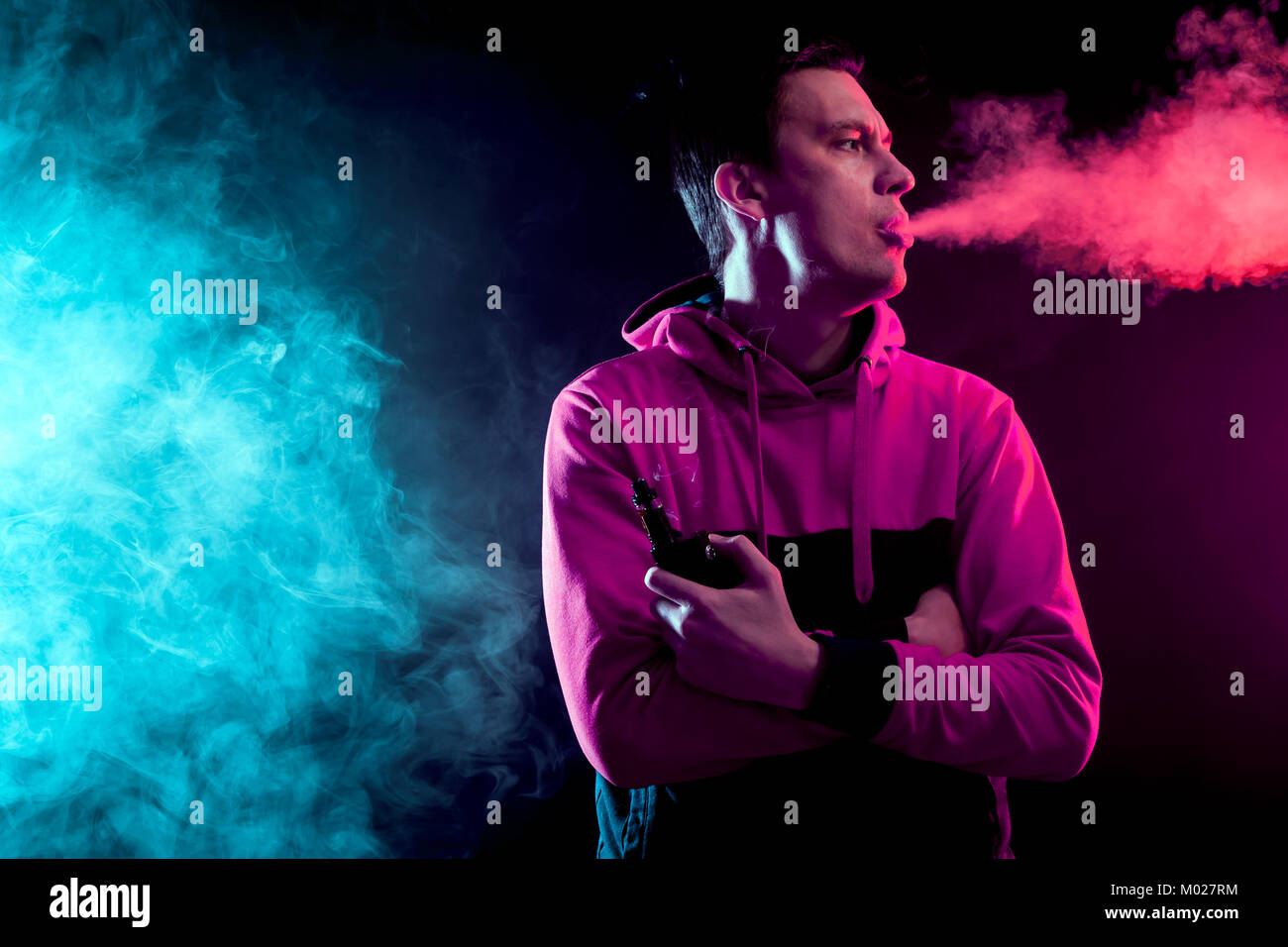Young stylish male smoker in a sweatshirt is smoking a vape, and around ...