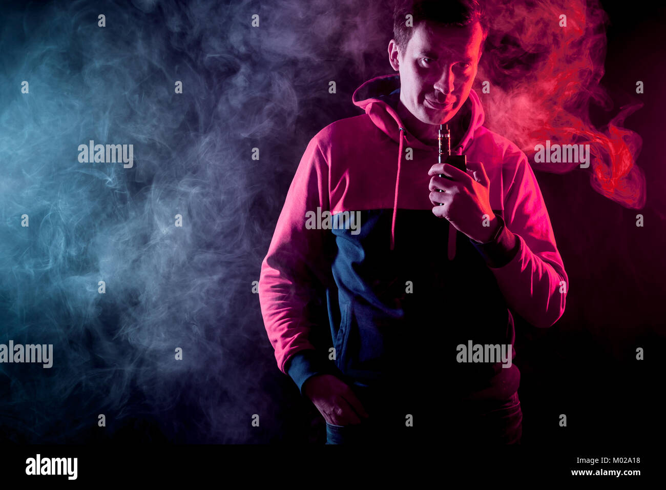Man in sport hoody vaping an electronic cigarette.Isolated on black ...