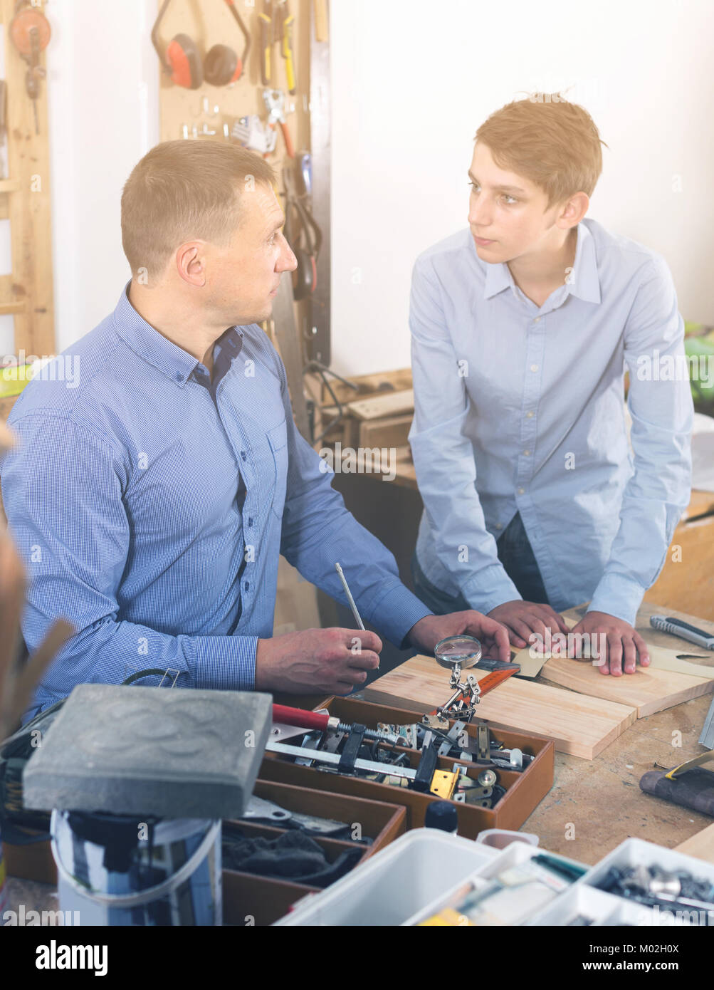happy russian father and teen son working with wood plank in workshop ...