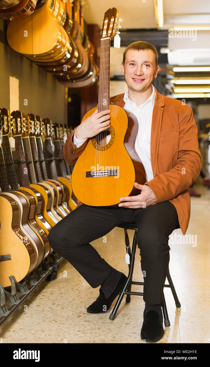 Smiling male customer deciding on acoustic guitar in musical shop Stock ...