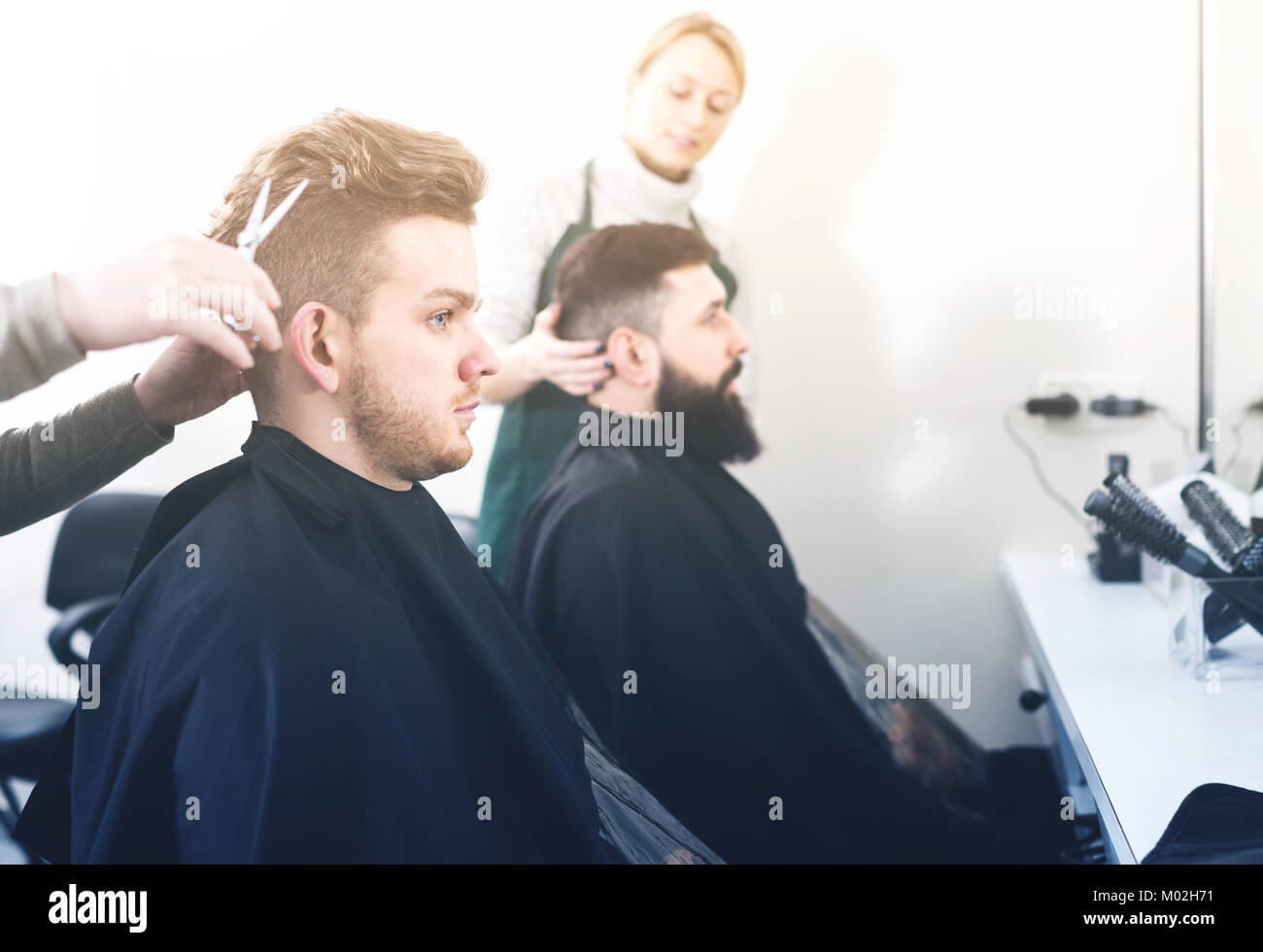 cheerful men clients waiting for their haircuts to be finished at hair ...