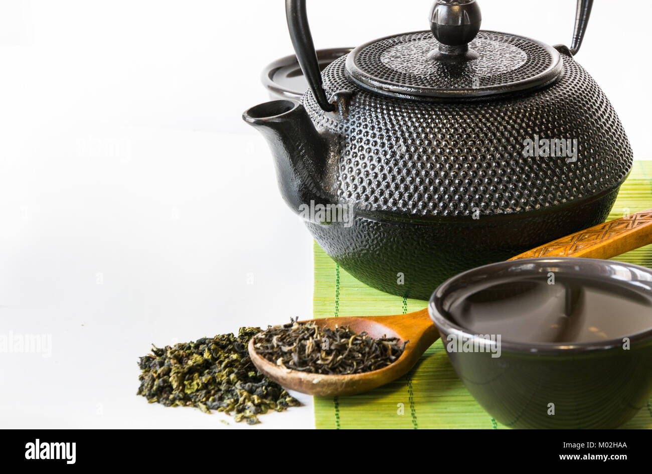 Asian green tea set on bamboo mat with dried green tea in spoon with ...