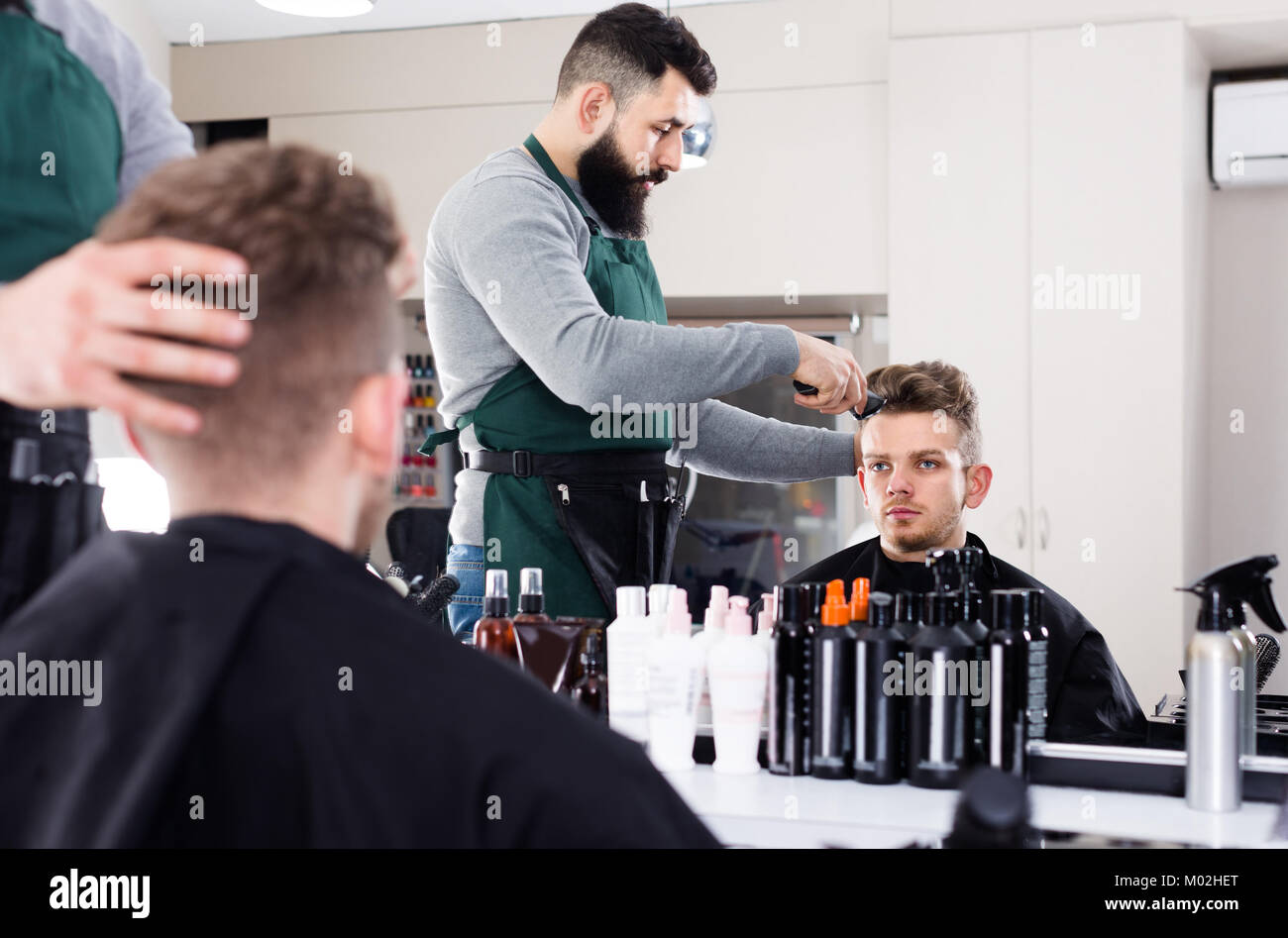 Young male stylist creating new haircut for man client at hairdressing ...