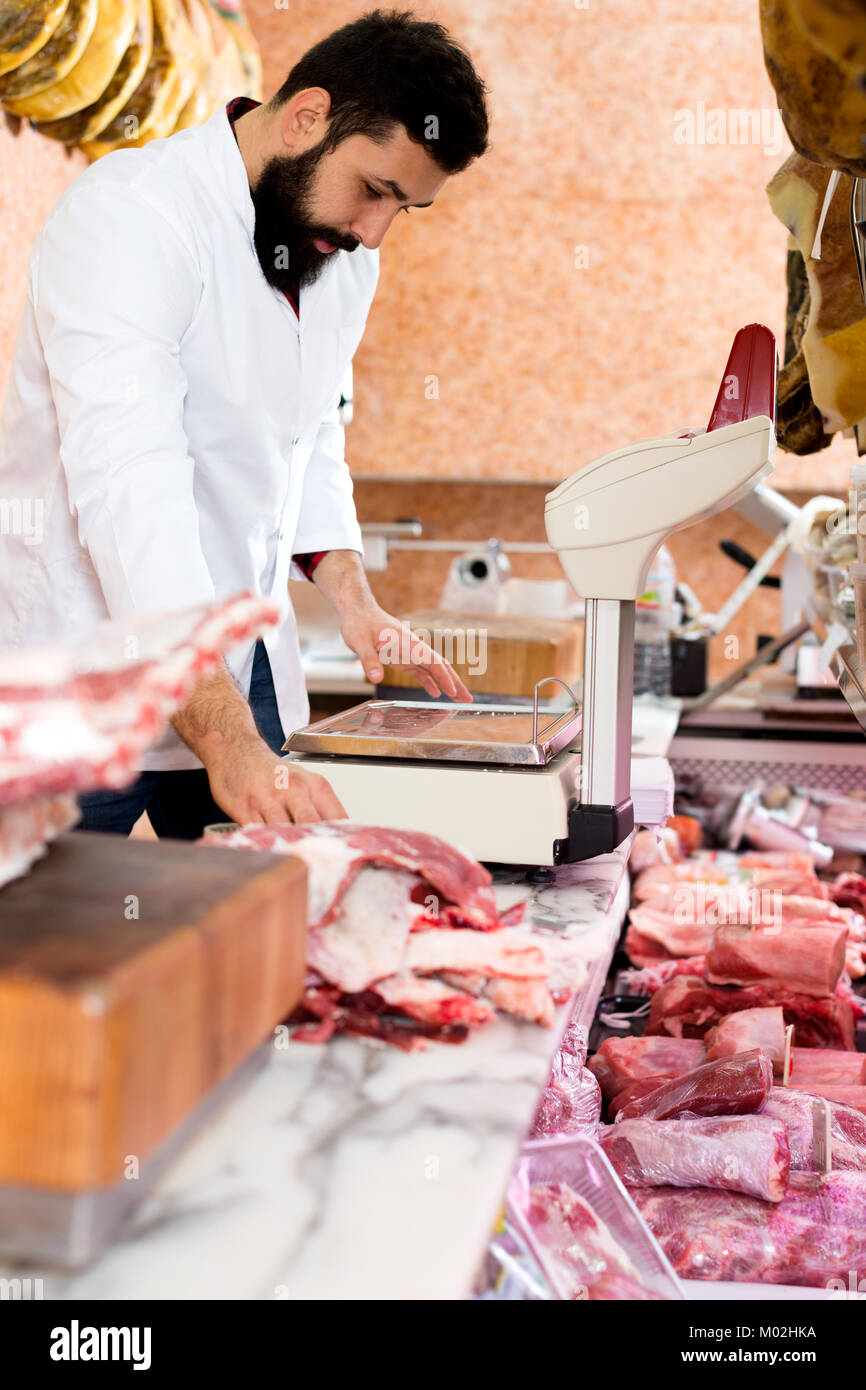 Glad young male seller cutting meat to sell in butcher’s shop Stock ...