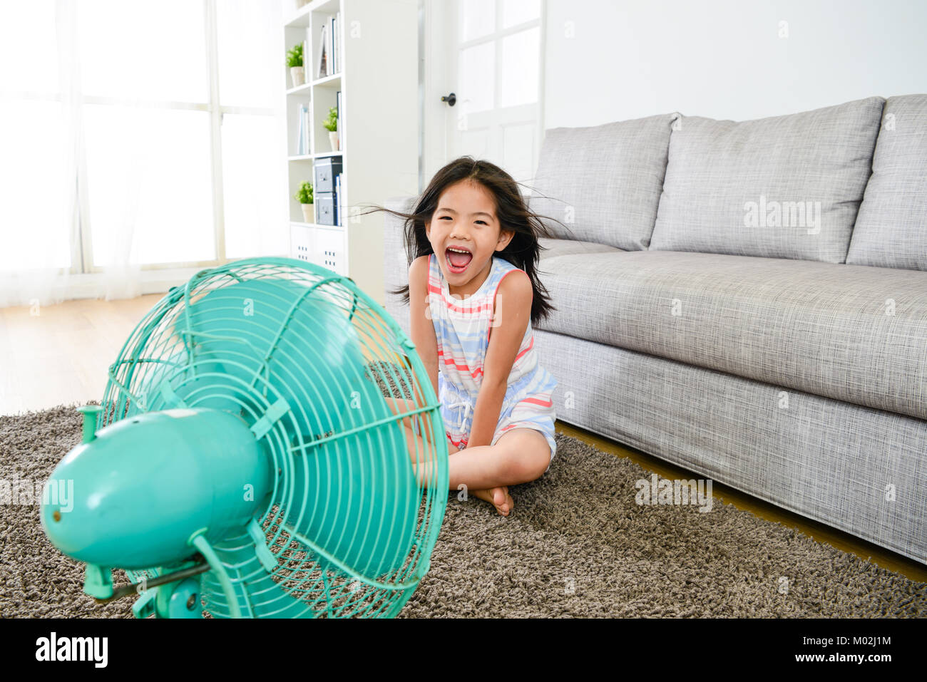 happy attractive female kid blowing cooling wind from electric fan ...