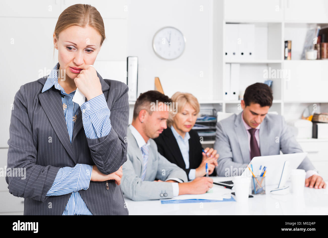Business woman crying standing in office with working colleagues behind ...