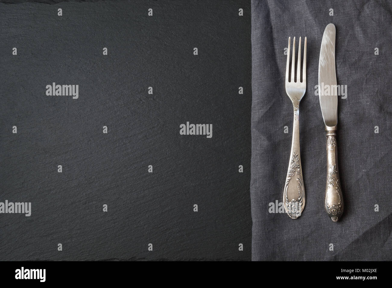 Rustic gray linen napkin, silverware and black slate dish with copy ...