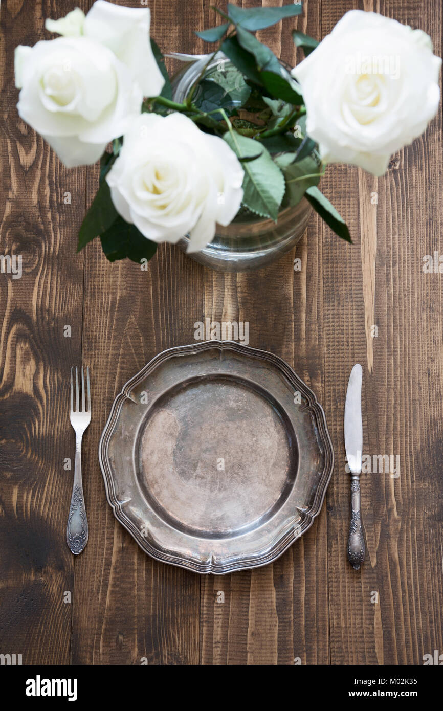 Romantic table setting with white rose, vintage dishware, silverware ...
