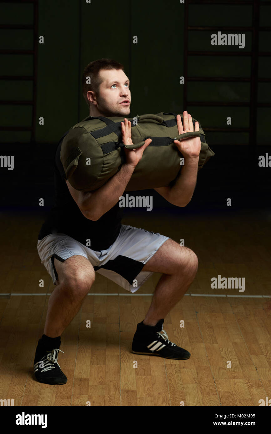 Man sqatting with sand weight bag on gym background Stock Photo - Alamy