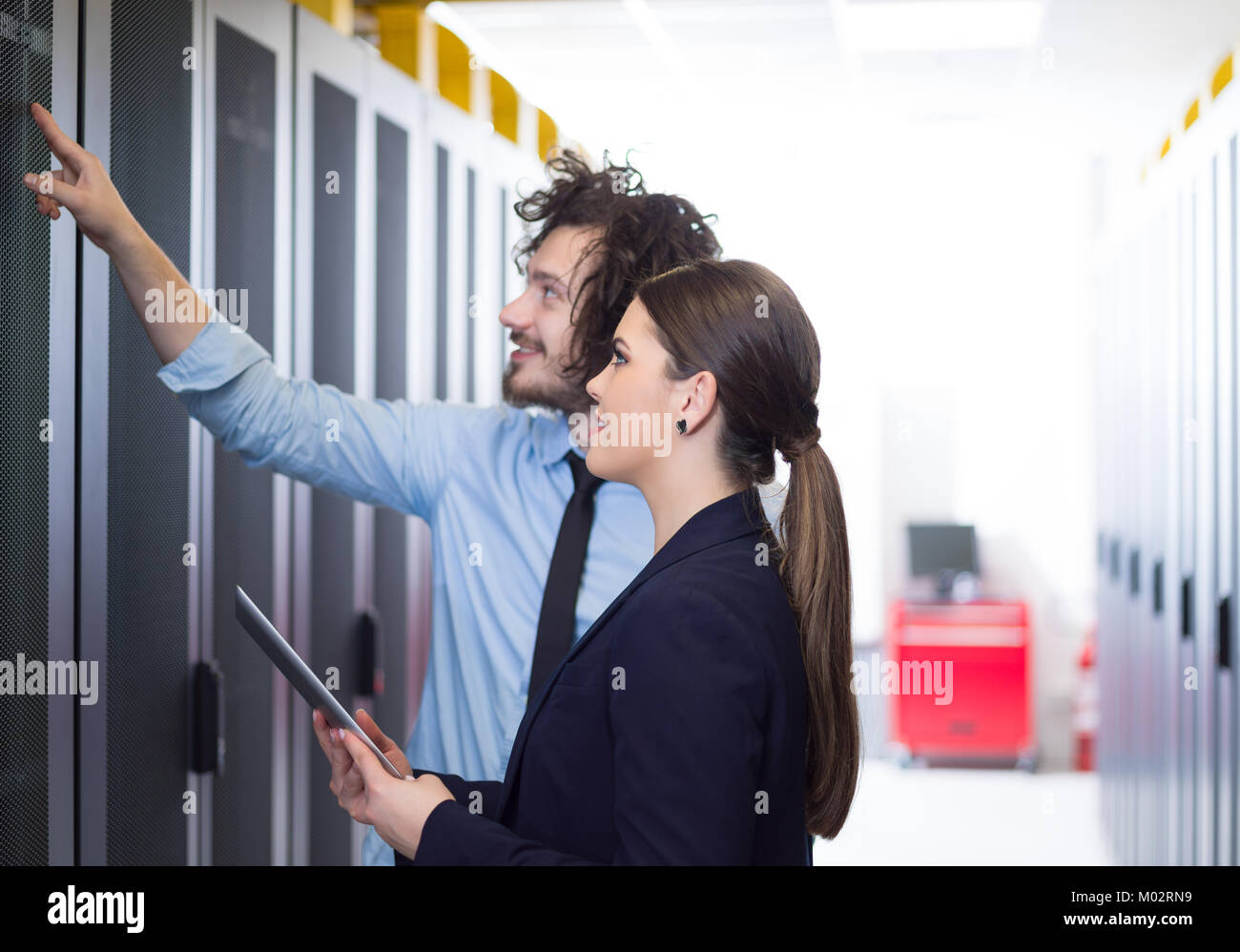 Young IT engineer showing working data center server room to female ...