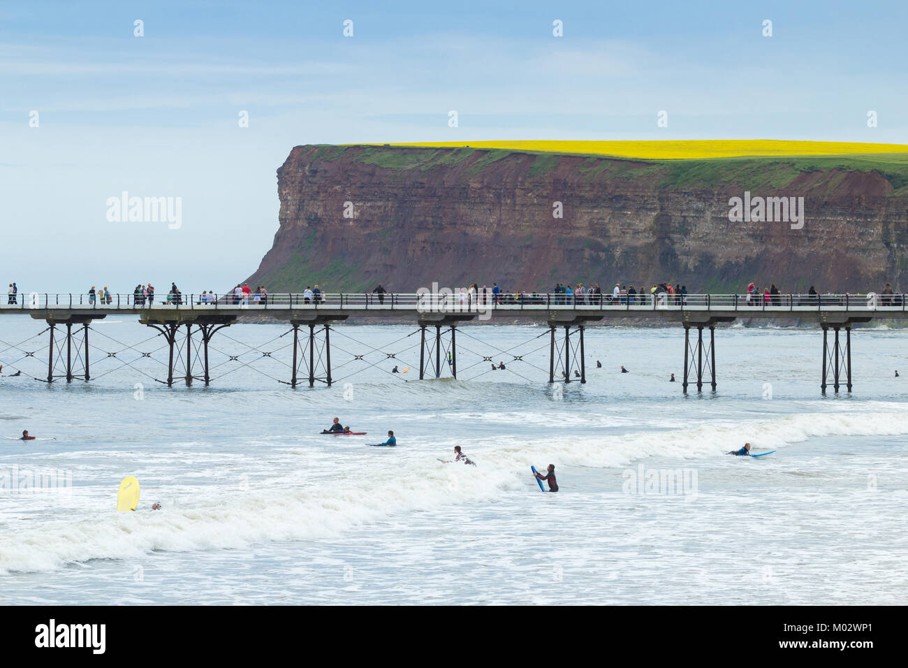 Surfers near Saltburn`s Victorian pier with walkers on cliff footpath ...