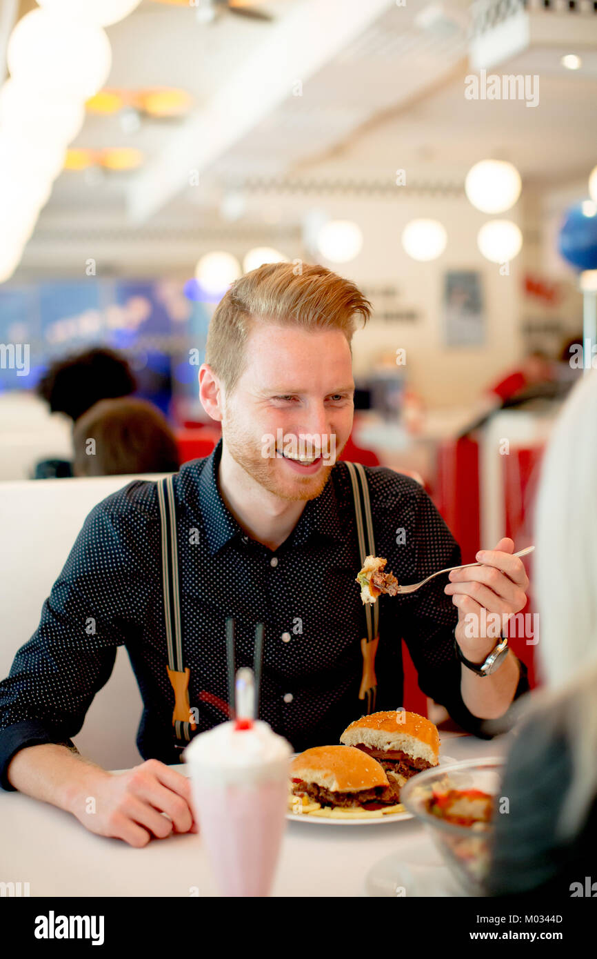 Young man eating beef cheeseburger in diner Stock Photo - Alamy