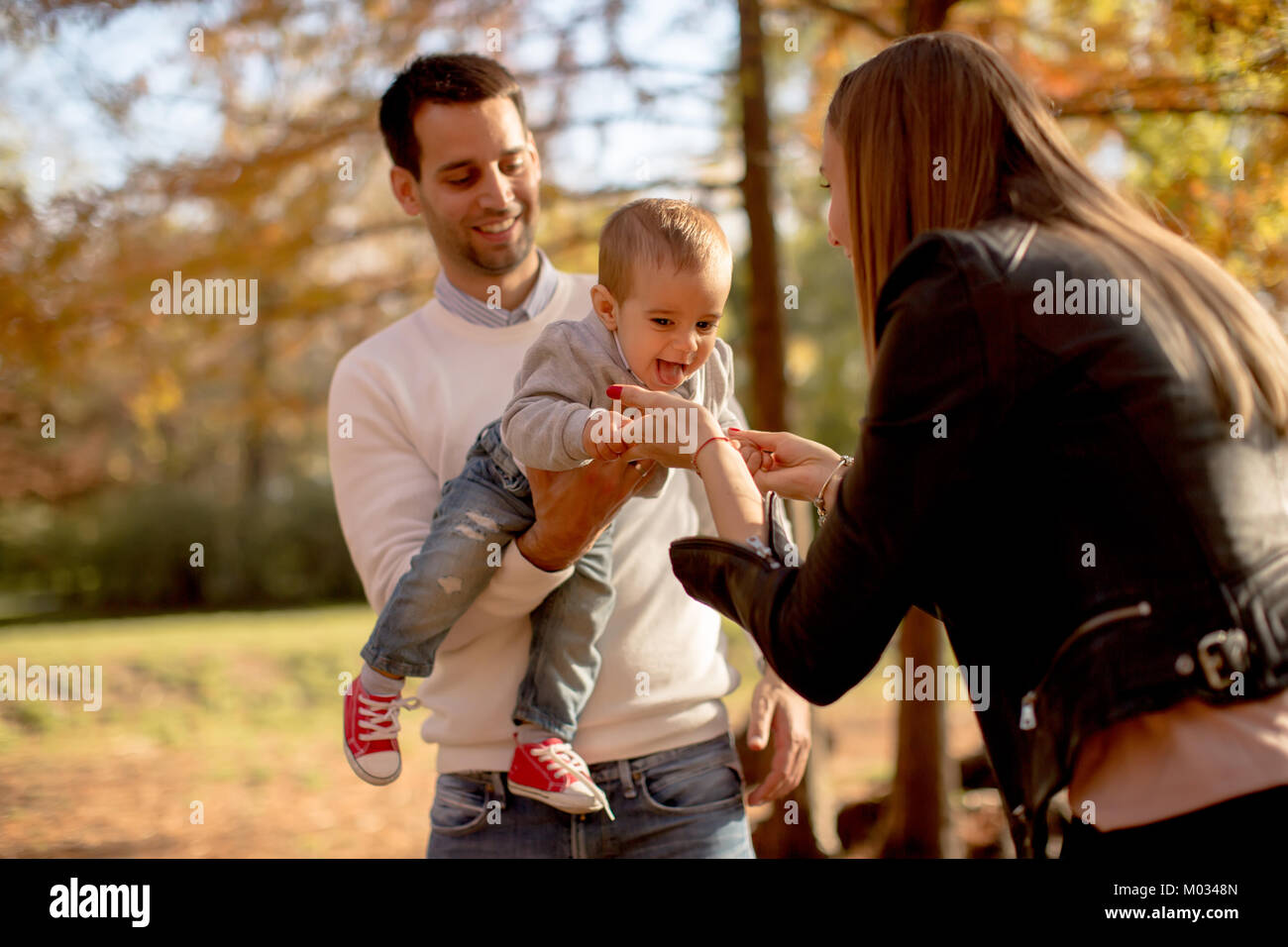 Happy young parents have fun with baby boy in autumn park Stock Photo ...