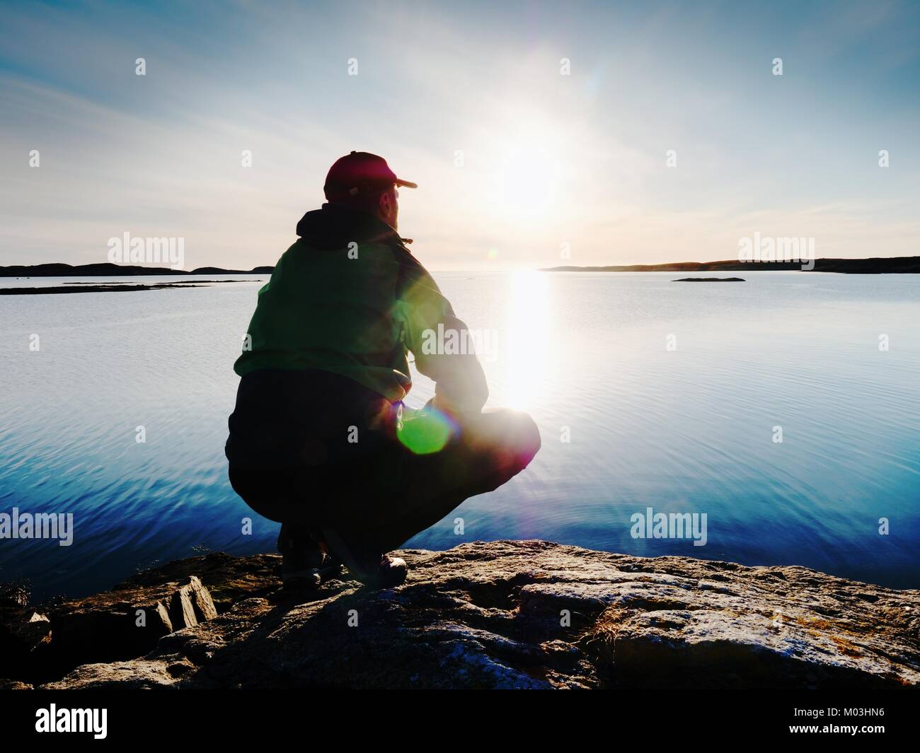Young man sitting on a rock watching a gorgeous sunset on the sea ...