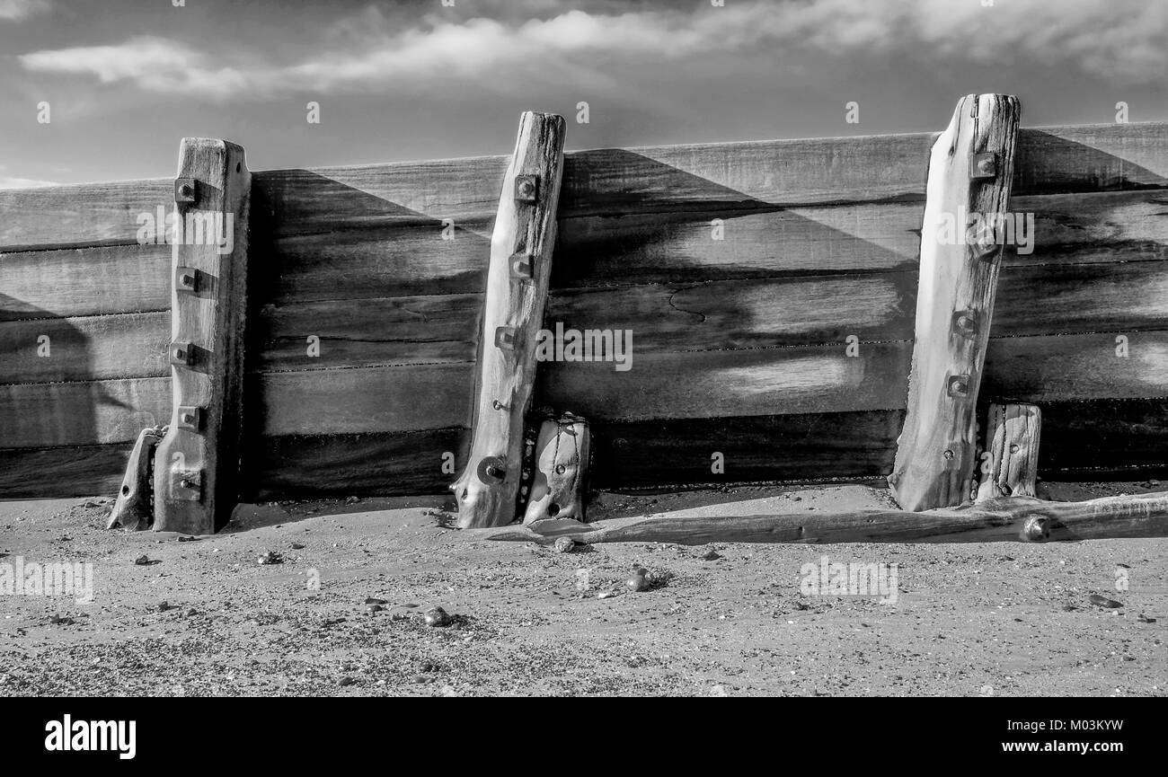 Wooden, weathered sea defence wall, four gnarled planks of wood running ...