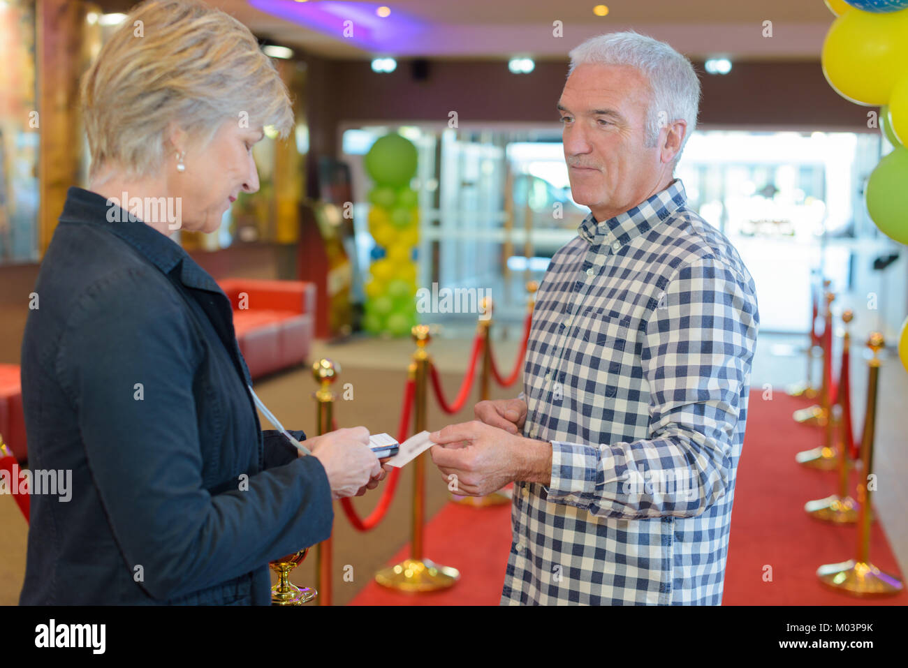 Man passing ticket to woman in lobby of theatre Stock Photo - Alamy