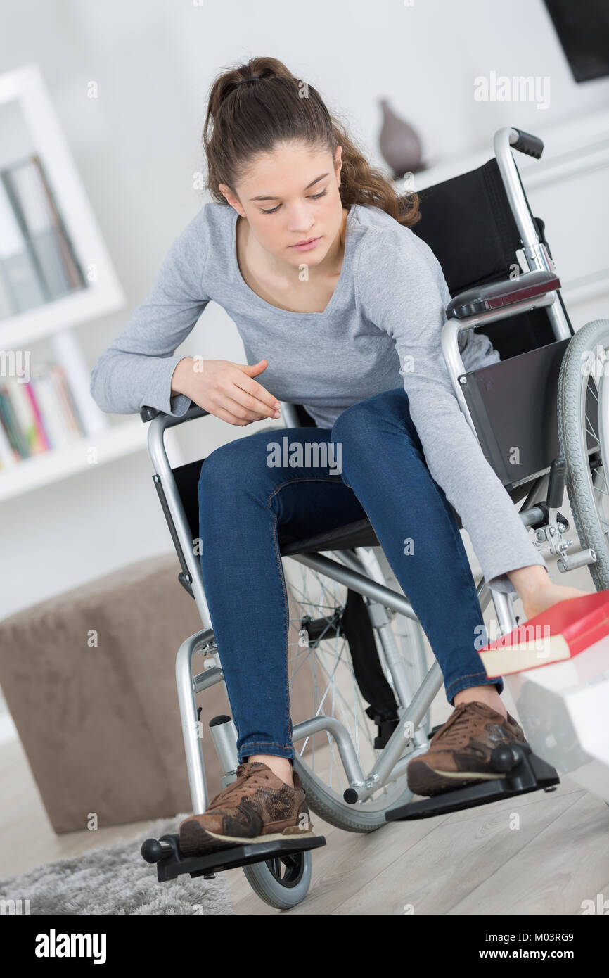 young woman sitting in wheelchair reaching a book Stock Photo - Alamy