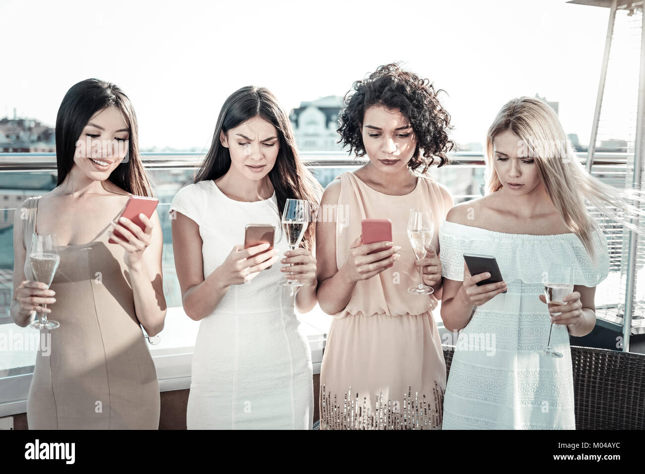 Good-looking cute girls messaging and keeping goblets of champagne ...