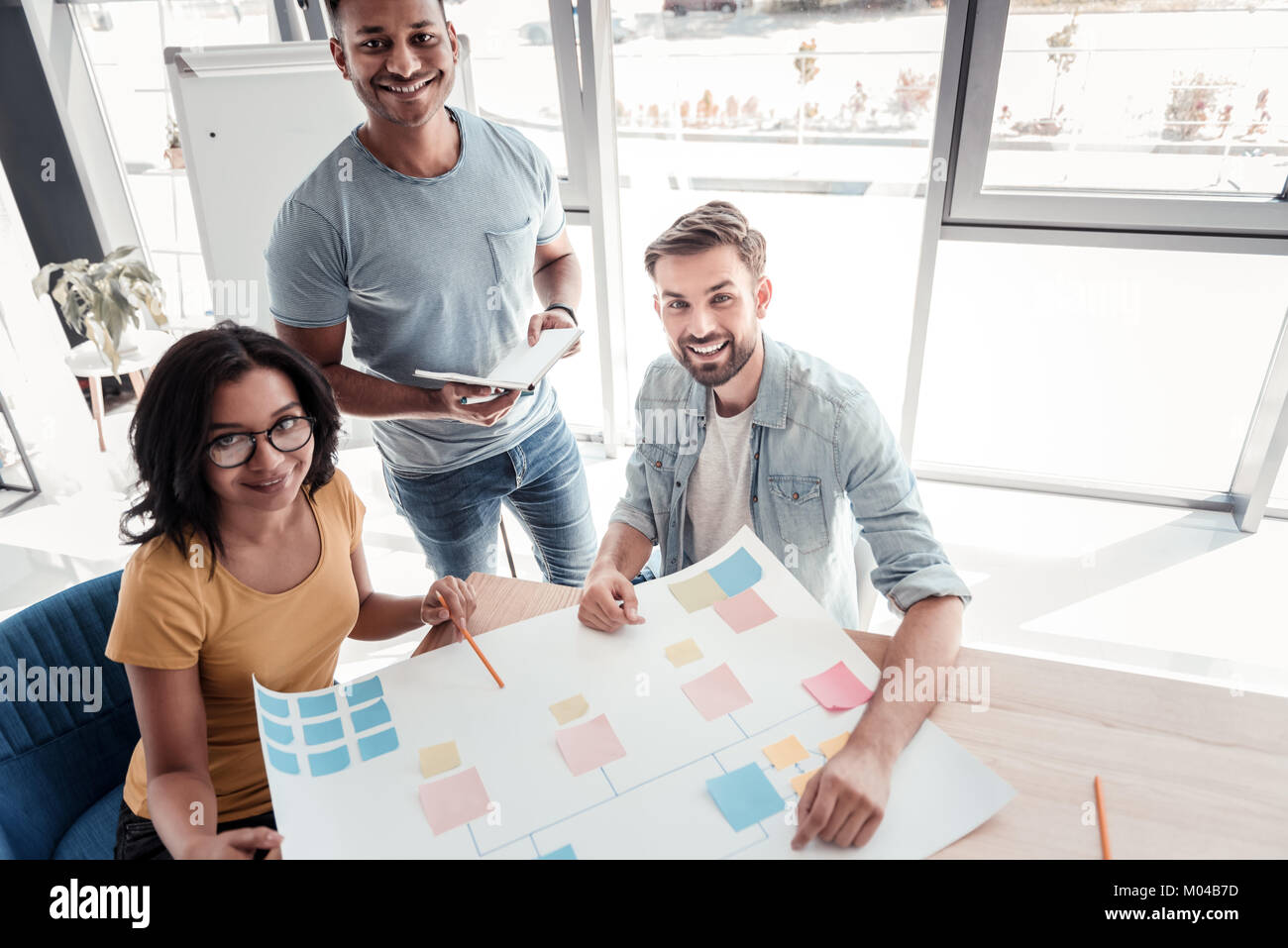 Cheerful young colleagues helping each other with project Stock Photo ...