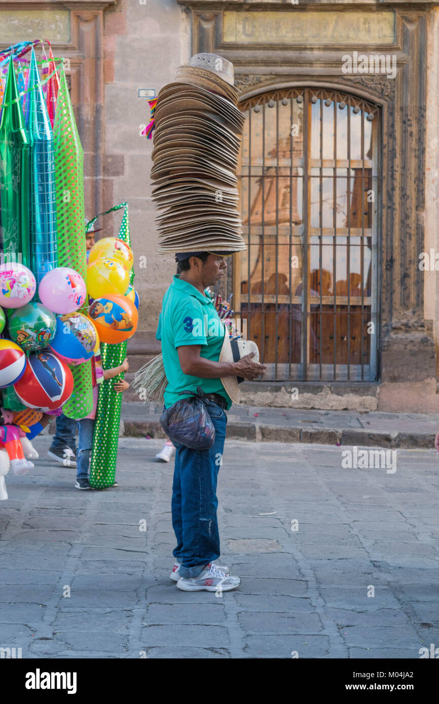 Male street vendor standing on a stone street with a tall stack of ...