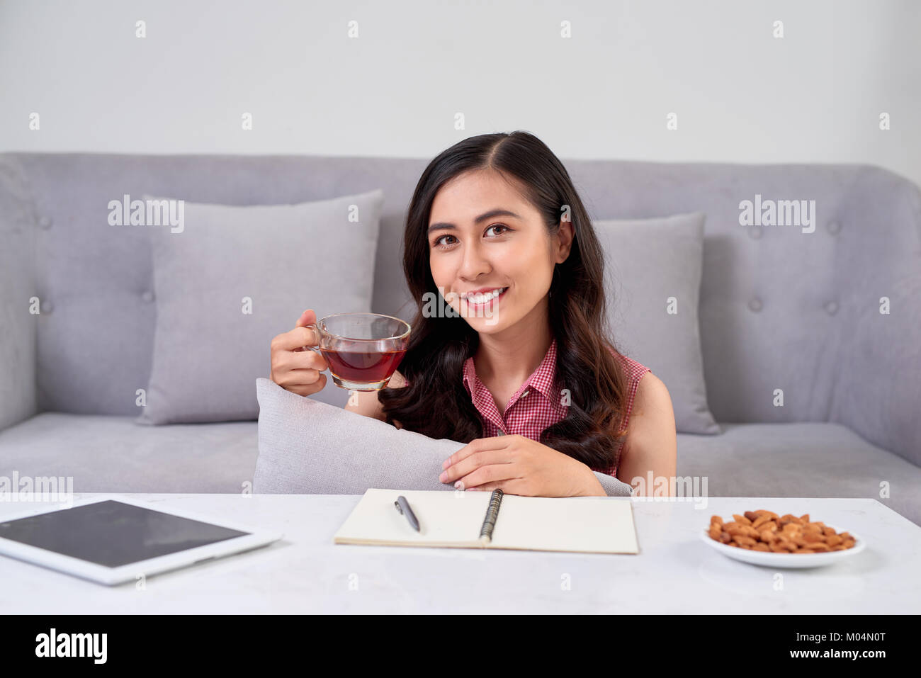 Young asian woman enjoying a tea break and snack while working at home ...