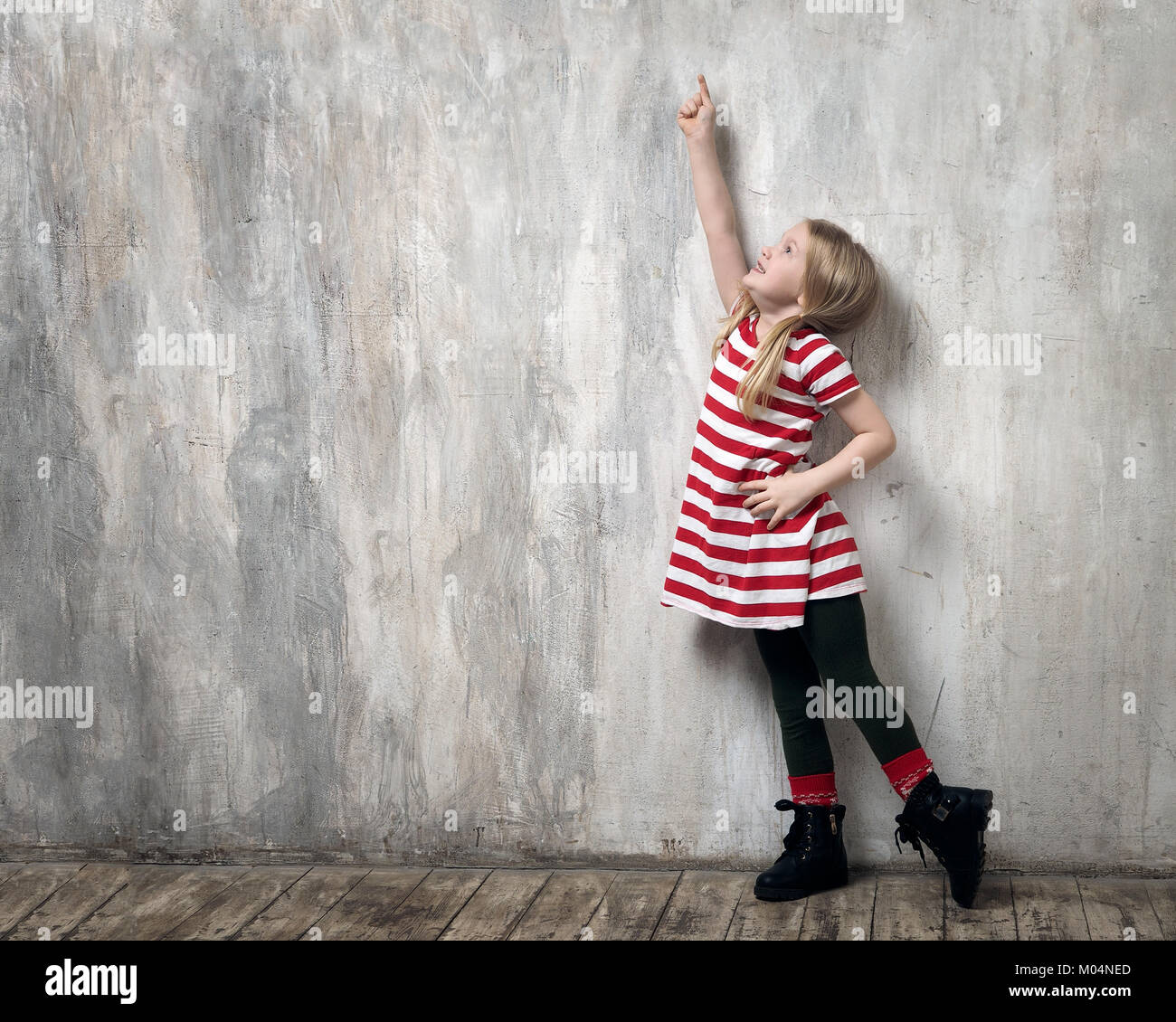 Joyful girl pulled high up making the hand gesture. Textured grey wall ...