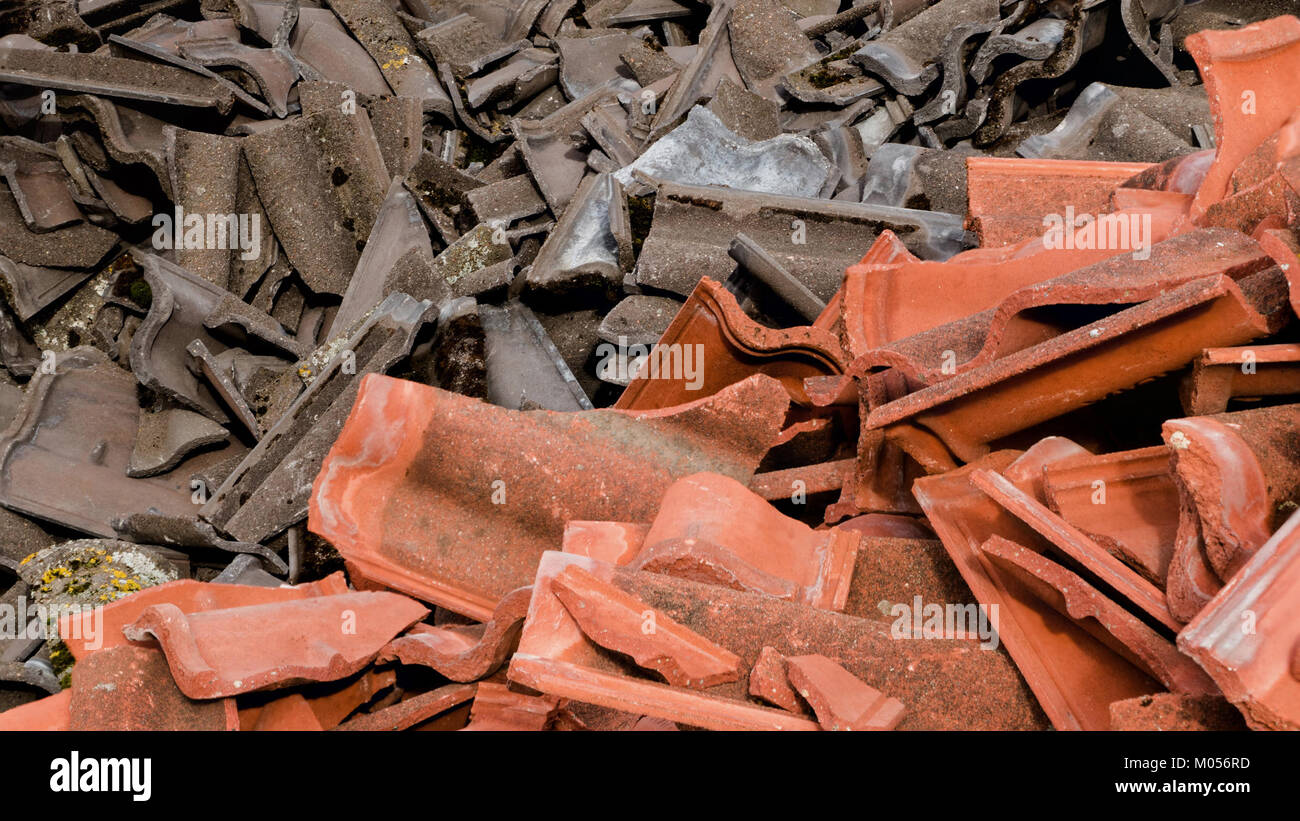 The image shows a collection of broken red and black roof tiles ...
