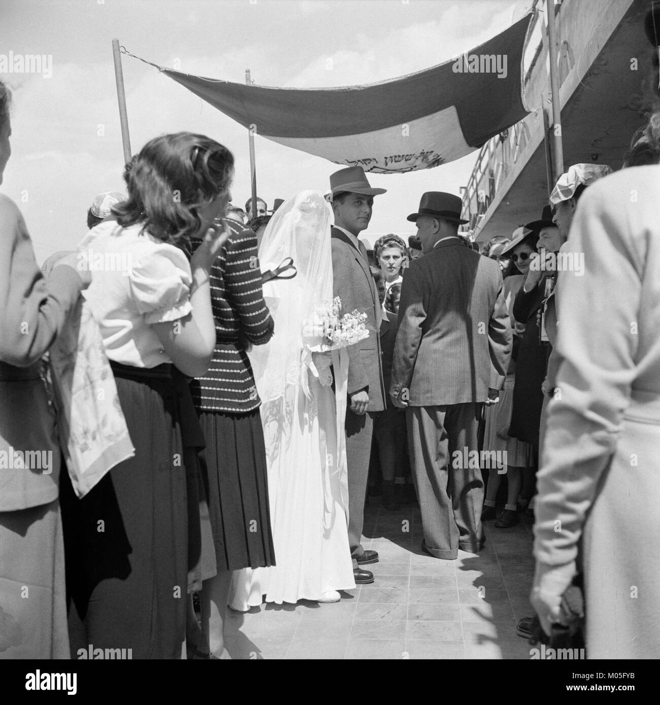 The image shows a wedding couple standing under a 'choopa', a canopy ...