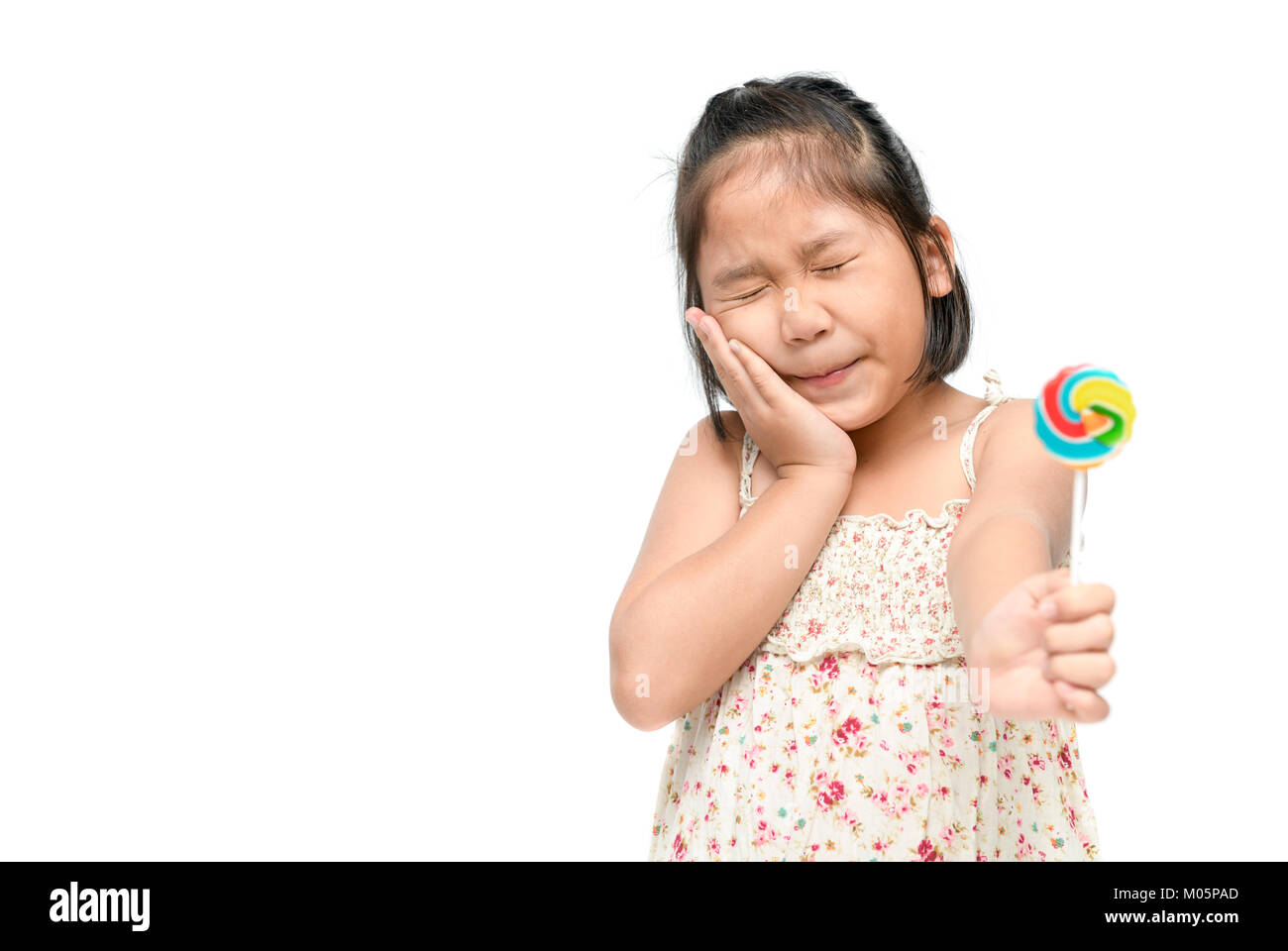 Little Asian girl suffering from toothache and holding candy in hand ...