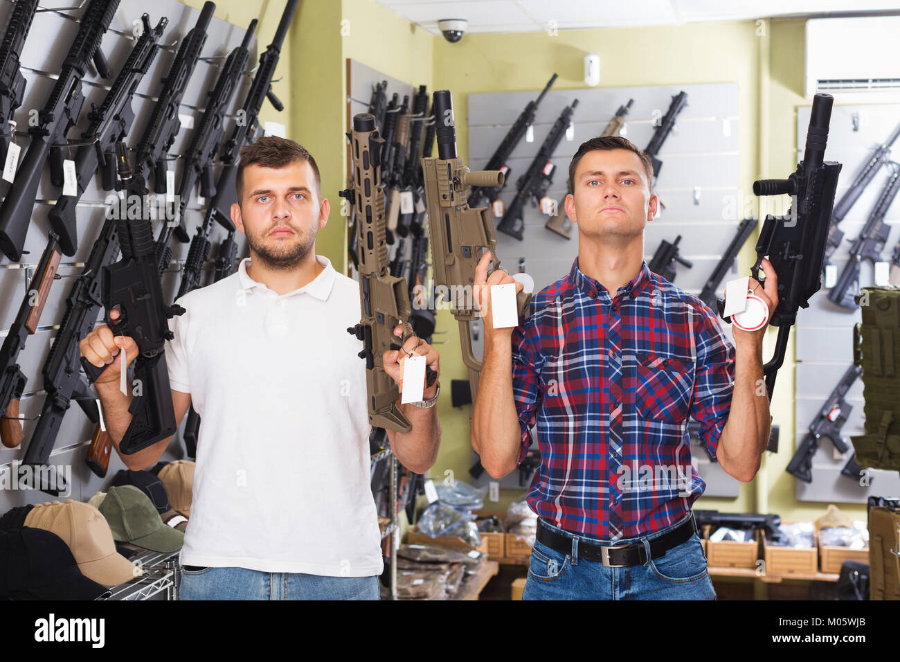 Portrait of two young male friends choosing air-powered gun in army ...