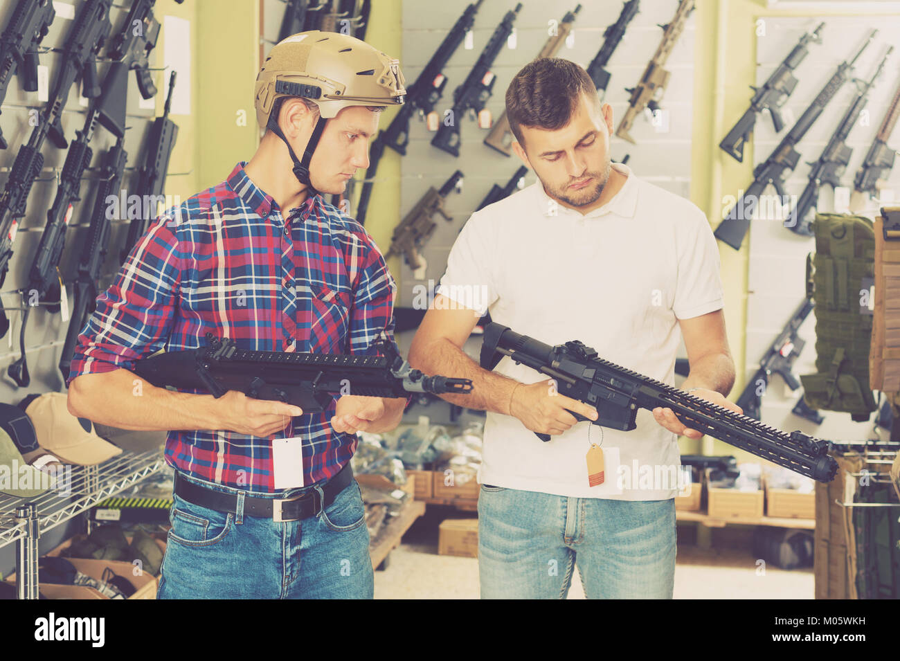 Portrait of two positive friends choosing air-powered gun in army ...