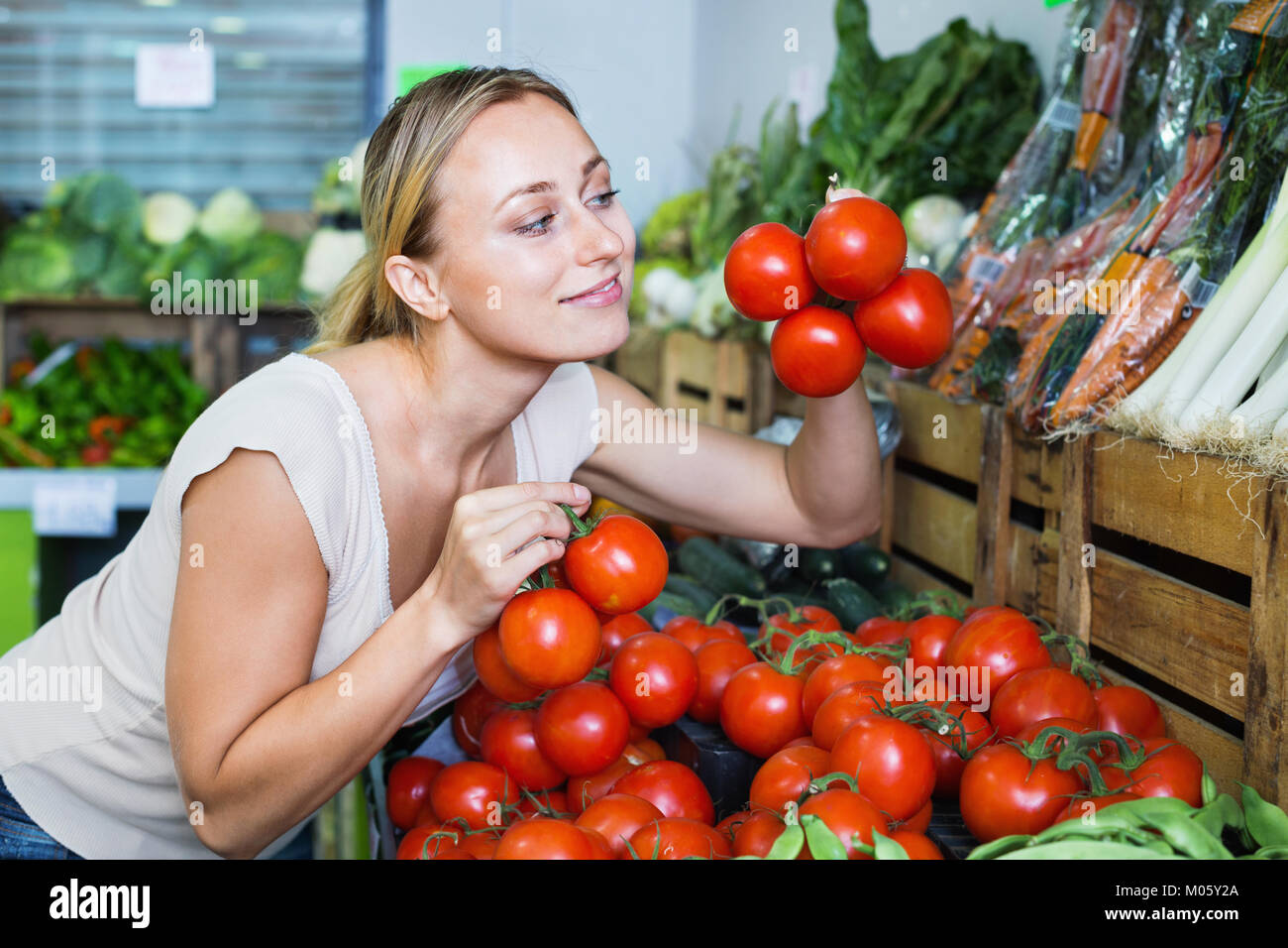 Portrait of young positive glad woman buying organic tomatoes in shop ...