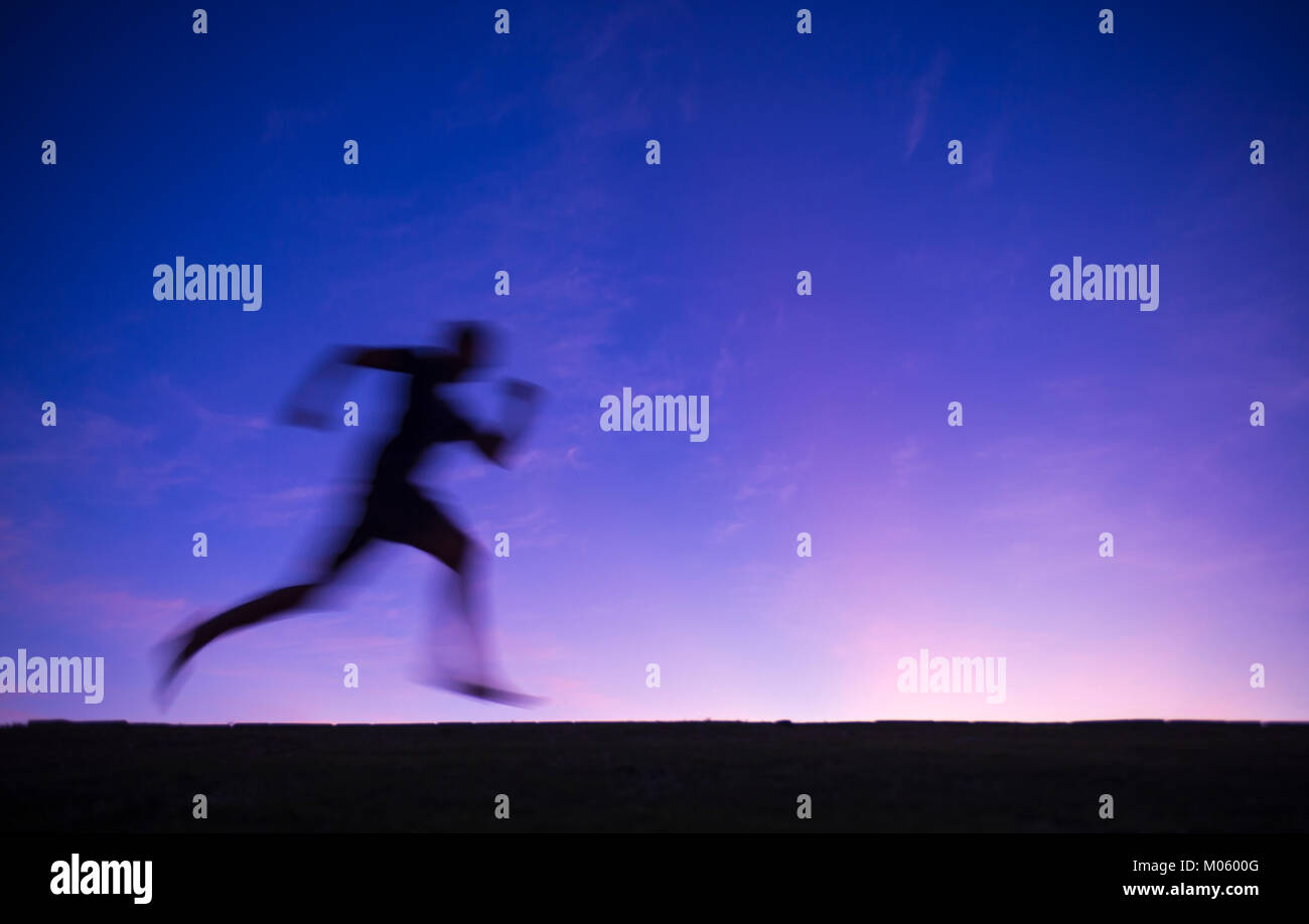 Silhouette blur of a runner passing across a purple twilight sunset sky ...