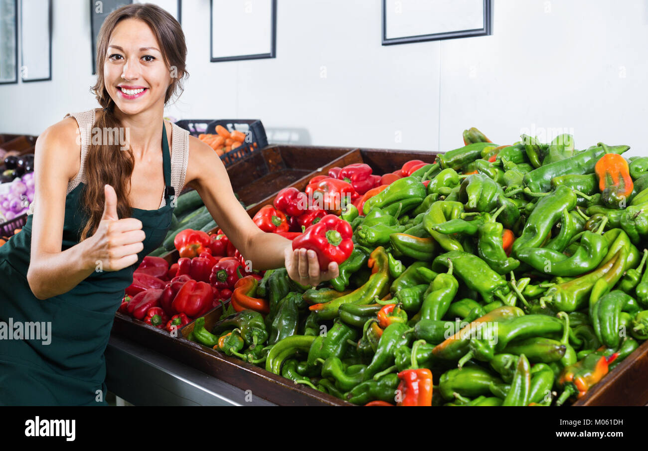 Positive smiling young woman seller wearing apron holding red and green ...