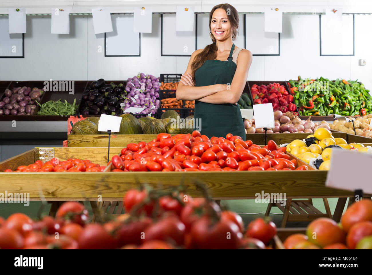 positive young woman seller showing fresh ripe tomatoes in food store ...