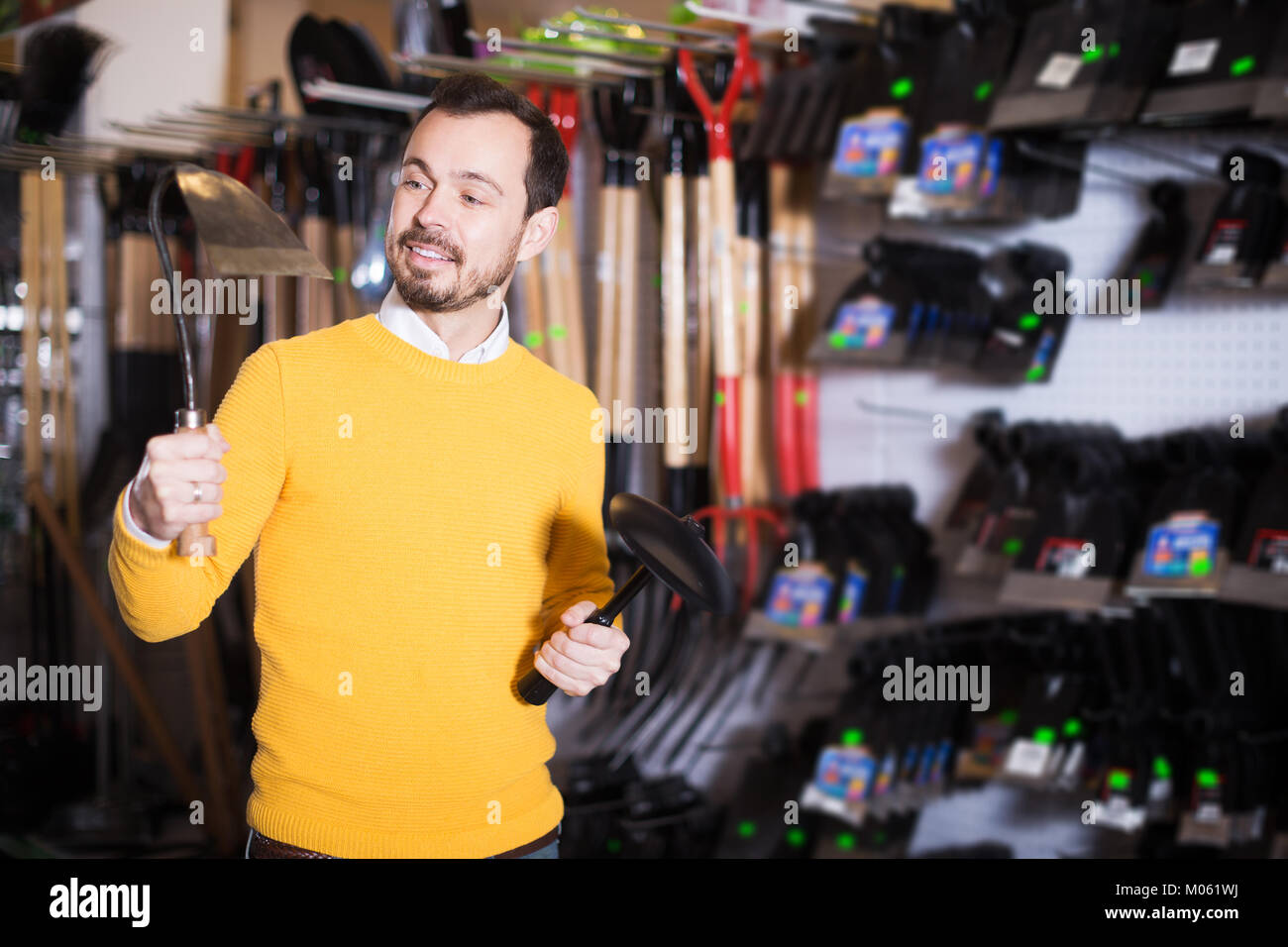 Smiling guy deciding on best tools in garden equipment shop Stock Photo ...