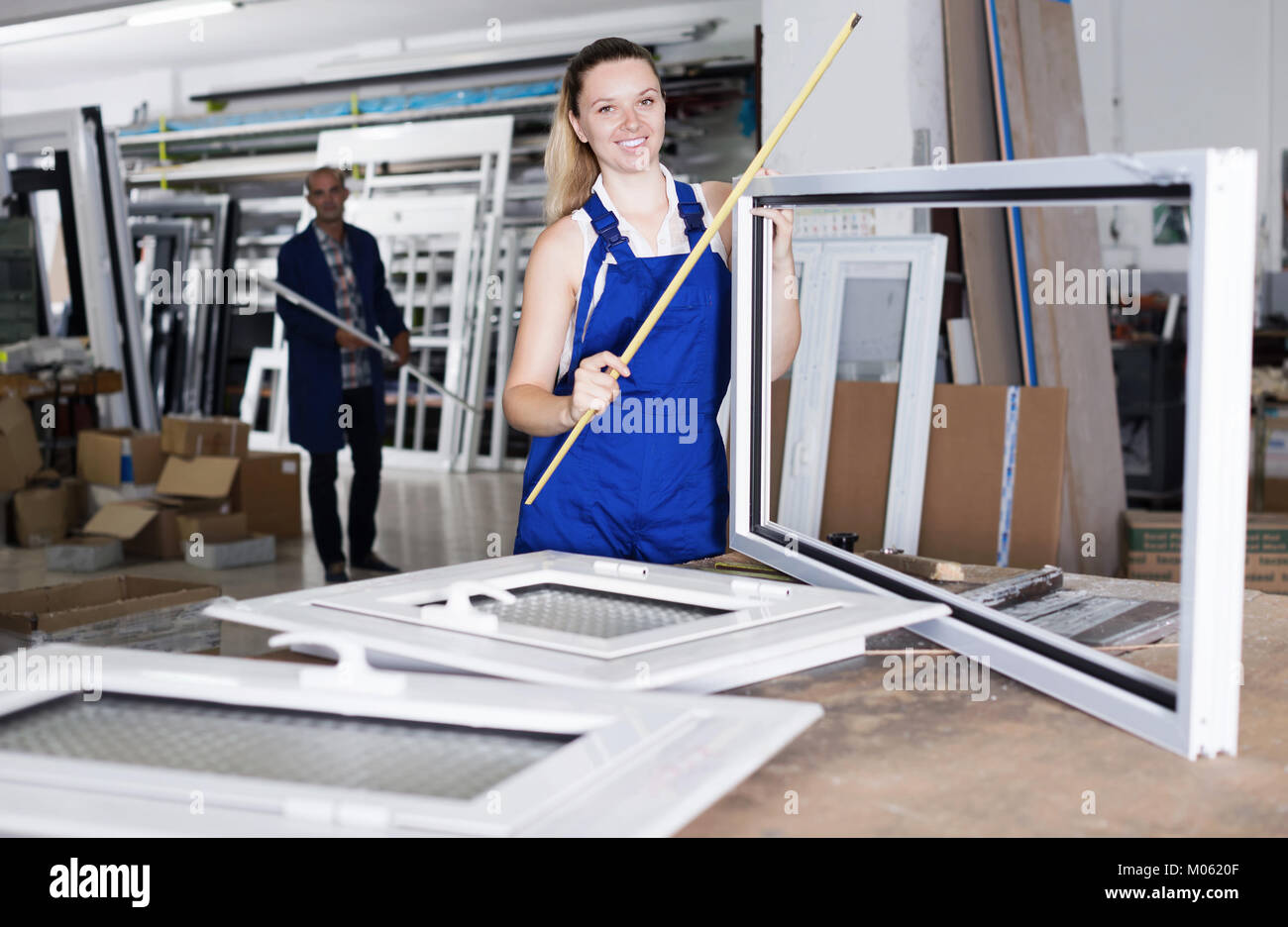 Young workwoman manufacturing plastic windows using measuring tape in ...
