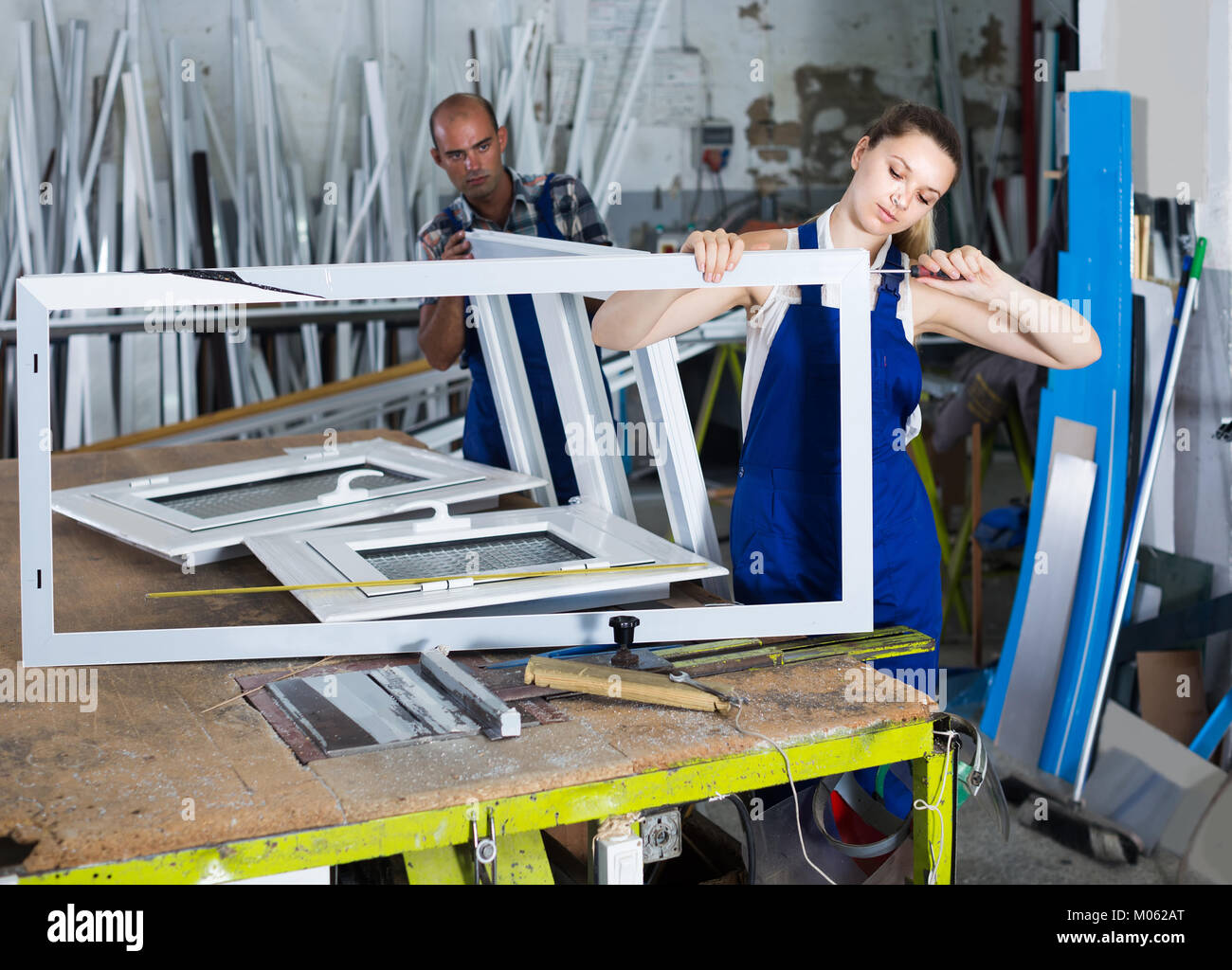 Young female worker assembling metal-plastic window in workshop, using ...