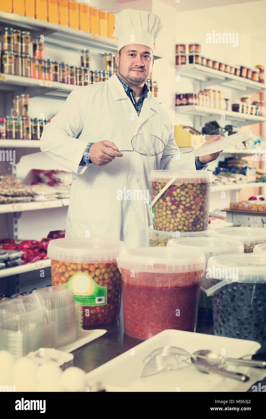 smiling salesman offering salted olives with filling in ordinary food ...
