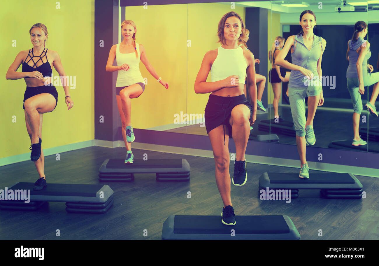 Group of smiling sporty women working out with steppers in fitness ...