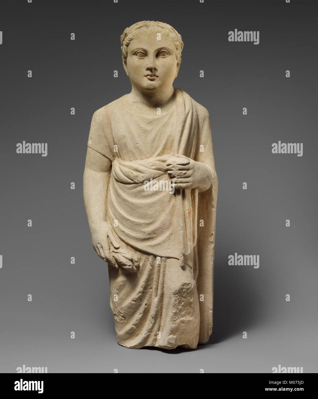 This limestone statuette portrays a boy holding a pyxis (a small box ...