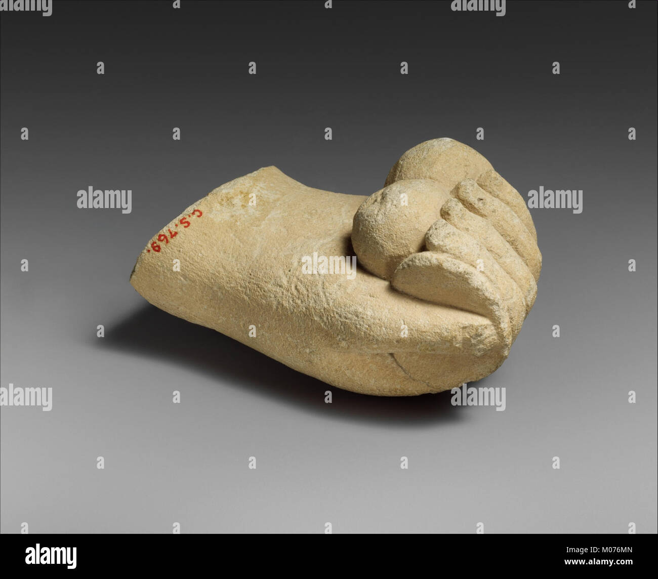 This limestone sculpture depicts a hand grasping a disk and several ...